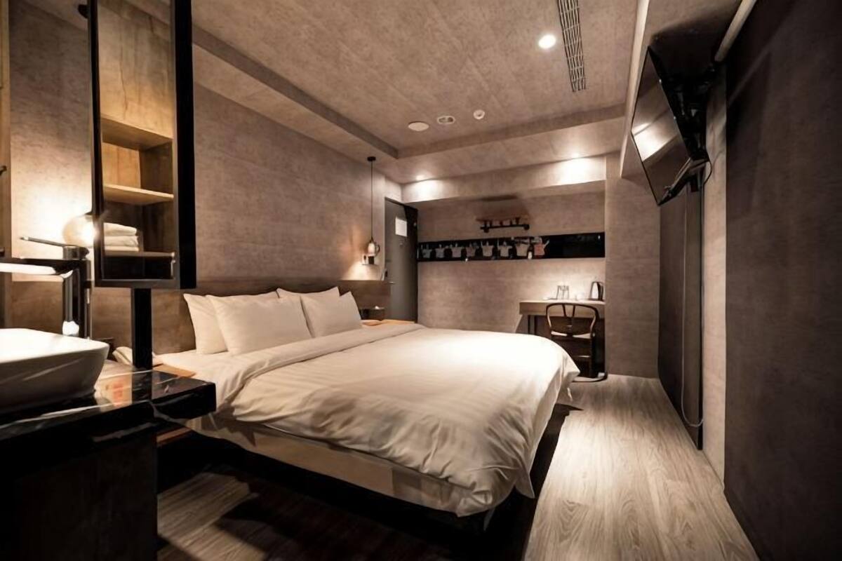 Quarto moderno com cama grande, mesas de cabeceira, prateleira embutida e televisão na parede.
