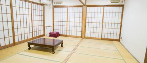 Um quarto japonês tradicional, com piso de tatame, portas corrediças e uma pequena mesa de madeira.