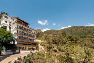 Um hotel com vários andares, com uma placa bem visível, localizado numa encosta com vista para uma área arborizada.