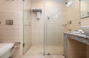 Casa de banho moderna com chuveiro envolto em vidro, sanita e bancada de granito com lavatório.