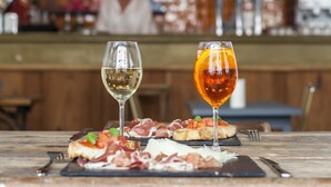 Interior de restaurante com balcão de madeira, duas taças de vinho e diversos pratos sobre a mesa.