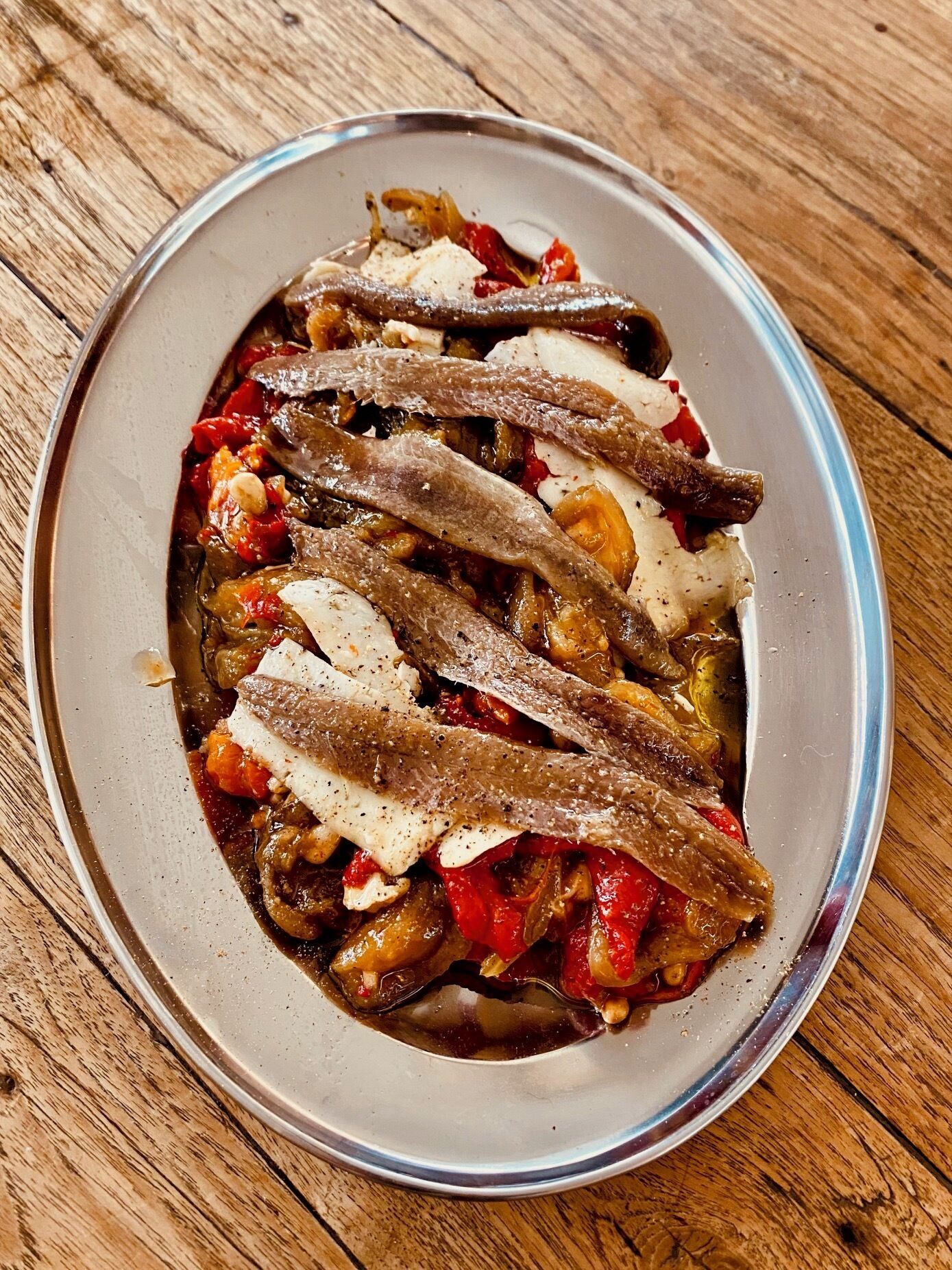 Prato de comida com peixe, legumes e queijo sobre uma mesa de madeira.