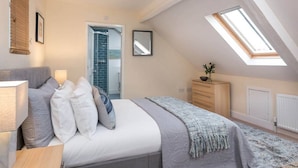 Quarto com cama, mesa de cabeceira, luminária, cômoda e claraboia.