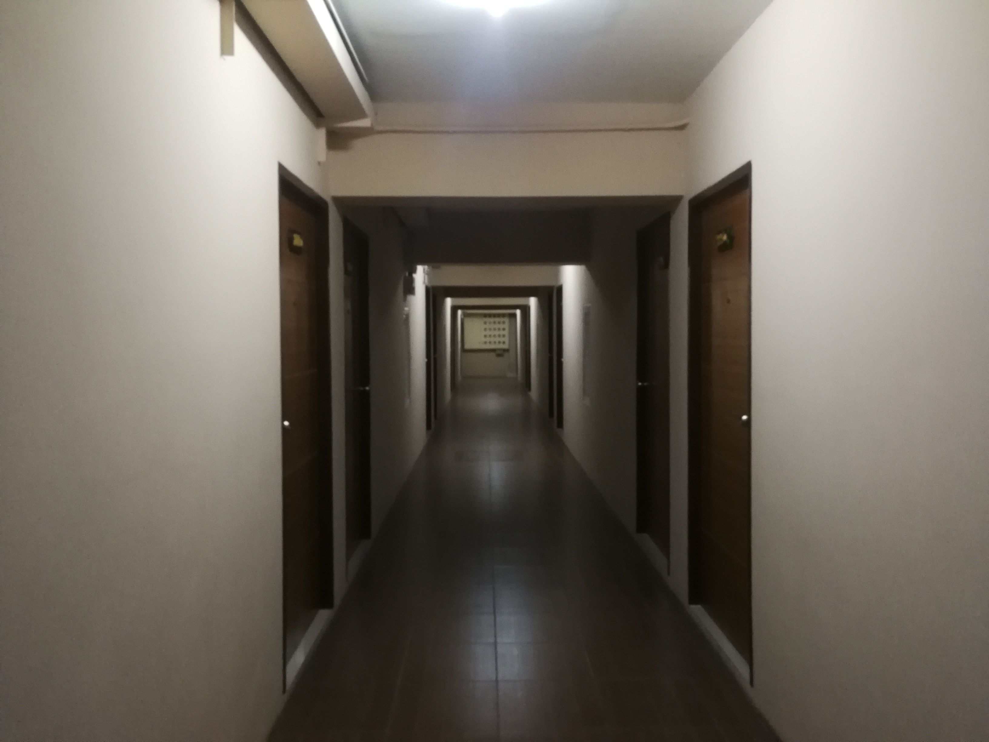 Um corredor comprido e estreito, com portas em ambos os lados que dão para quartos individuais.