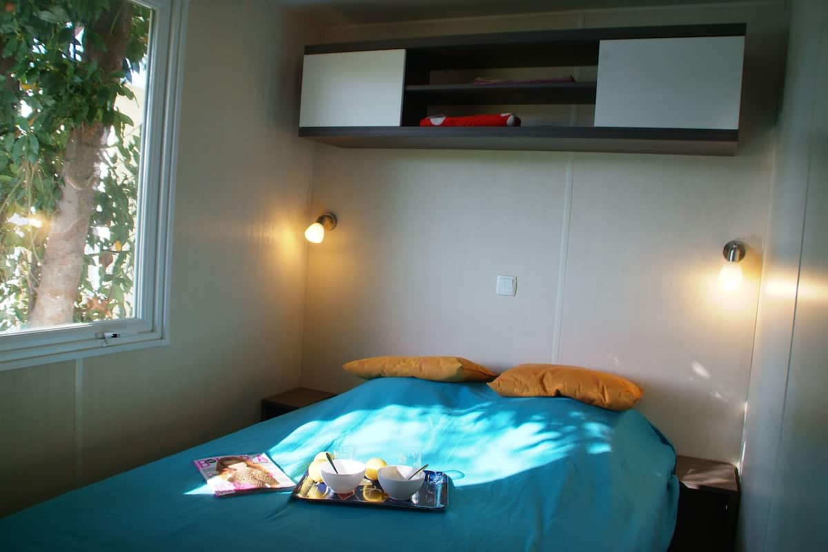 Quarto com cama, almofadas, bandeja com itens de café da manhã e prateleira sobre a cama.