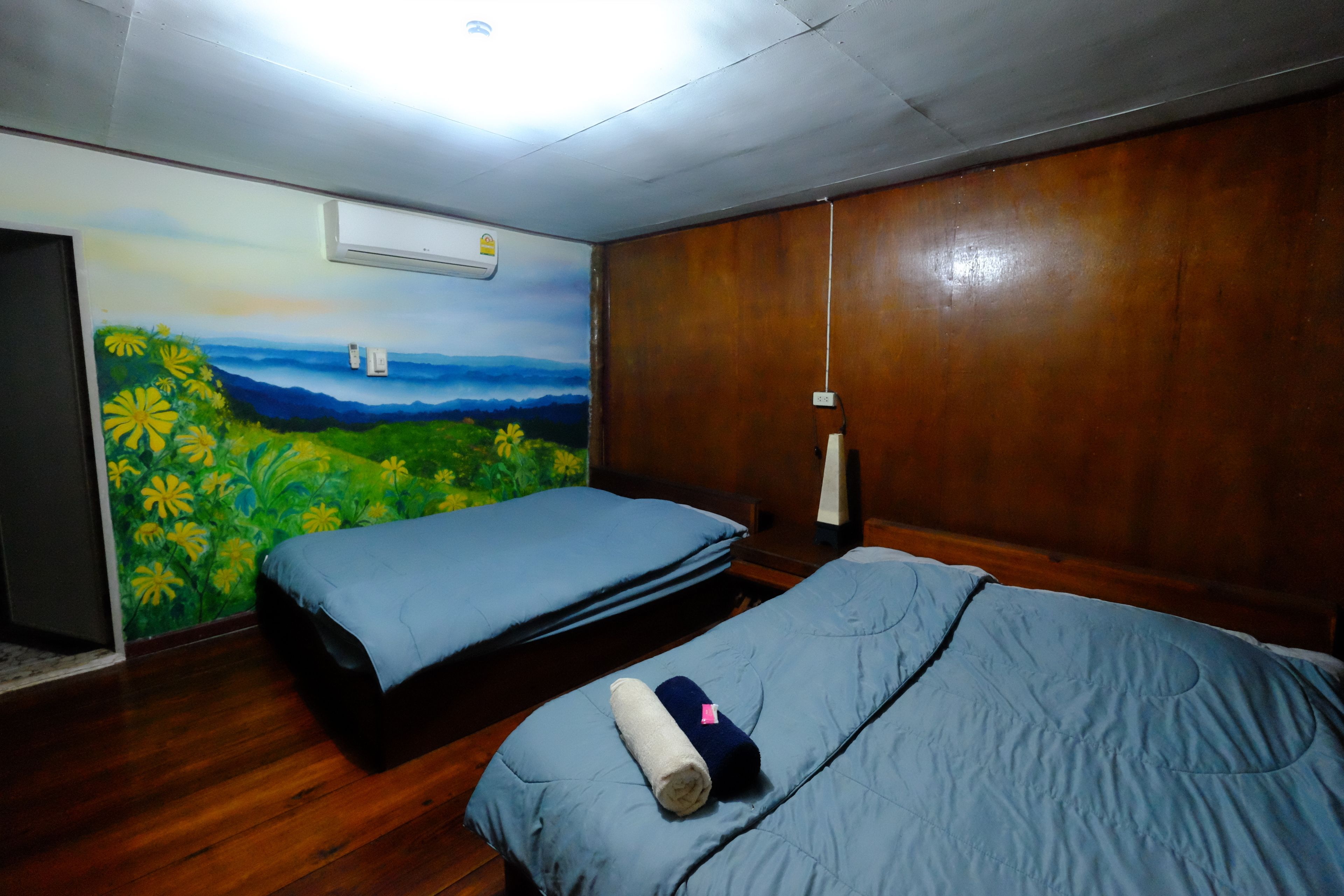 Quarto com duas camas, piso de madeira, um mural na parede e um aparelho de ar condicionado.