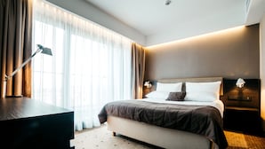Quarto de hotel moderno com uma cama grande, uma escrivaninha e uma luminária.