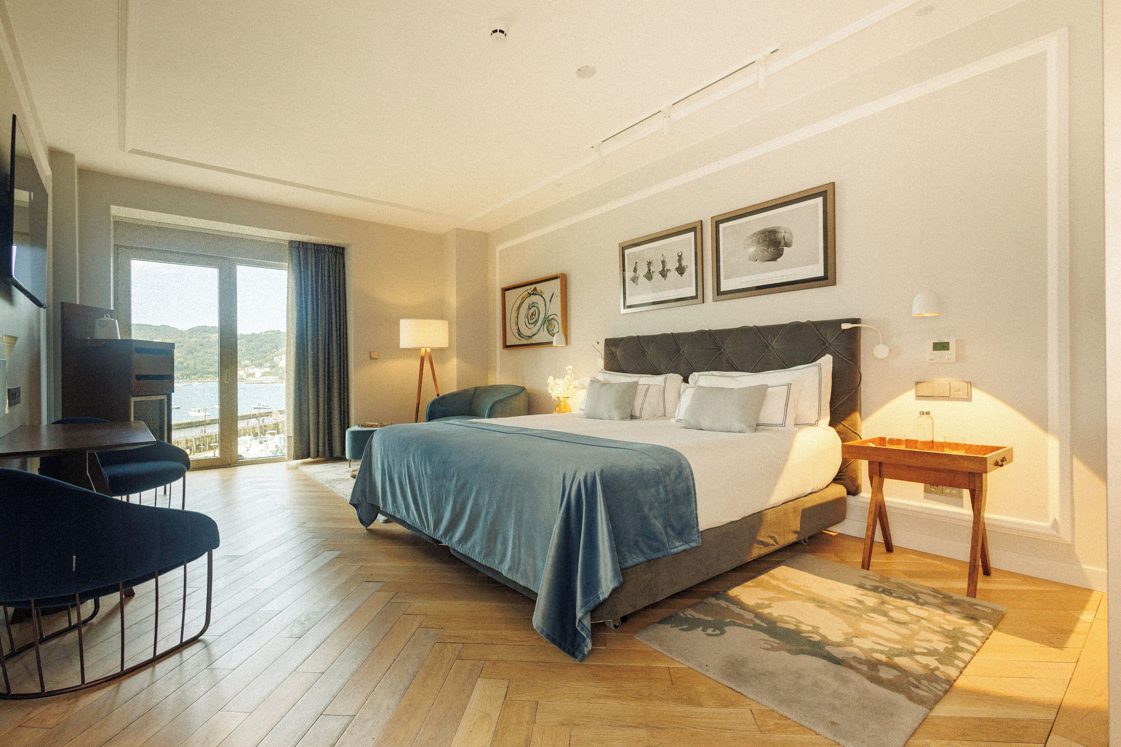 Quarto de hotel com cama, secretária e cadeira. Tem uma janela com vista para o exterior.