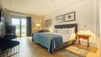 Quarto de hotel com cama, secretária e cadeira. Tem uma janela com vista para o exterior.