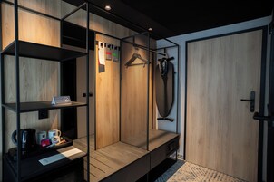 Quarto de hotel moderno com guarda-roupa de madeira, uma escrivaninha com cafeteira e área de chuveiro.
