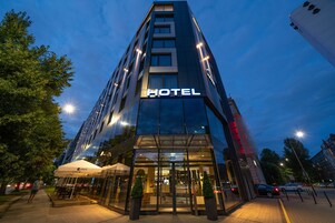 Um hotel moderno com fachada de vidro, entrada visível e área externa com guarda-sóis.