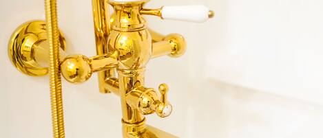 Um acessório dourado para banheiro, com chuveiro manual e torneira separada.