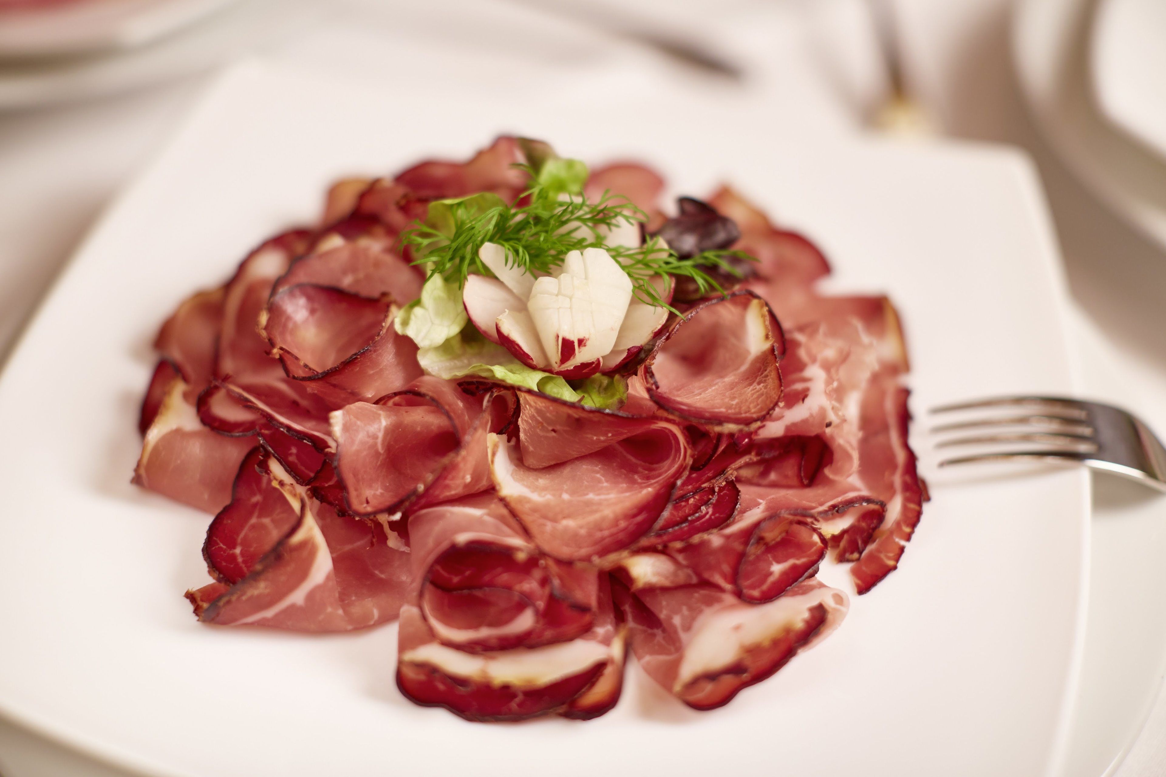 Um prato de carne curada em fatias, decorado com ervas e um rabanete pequeno.