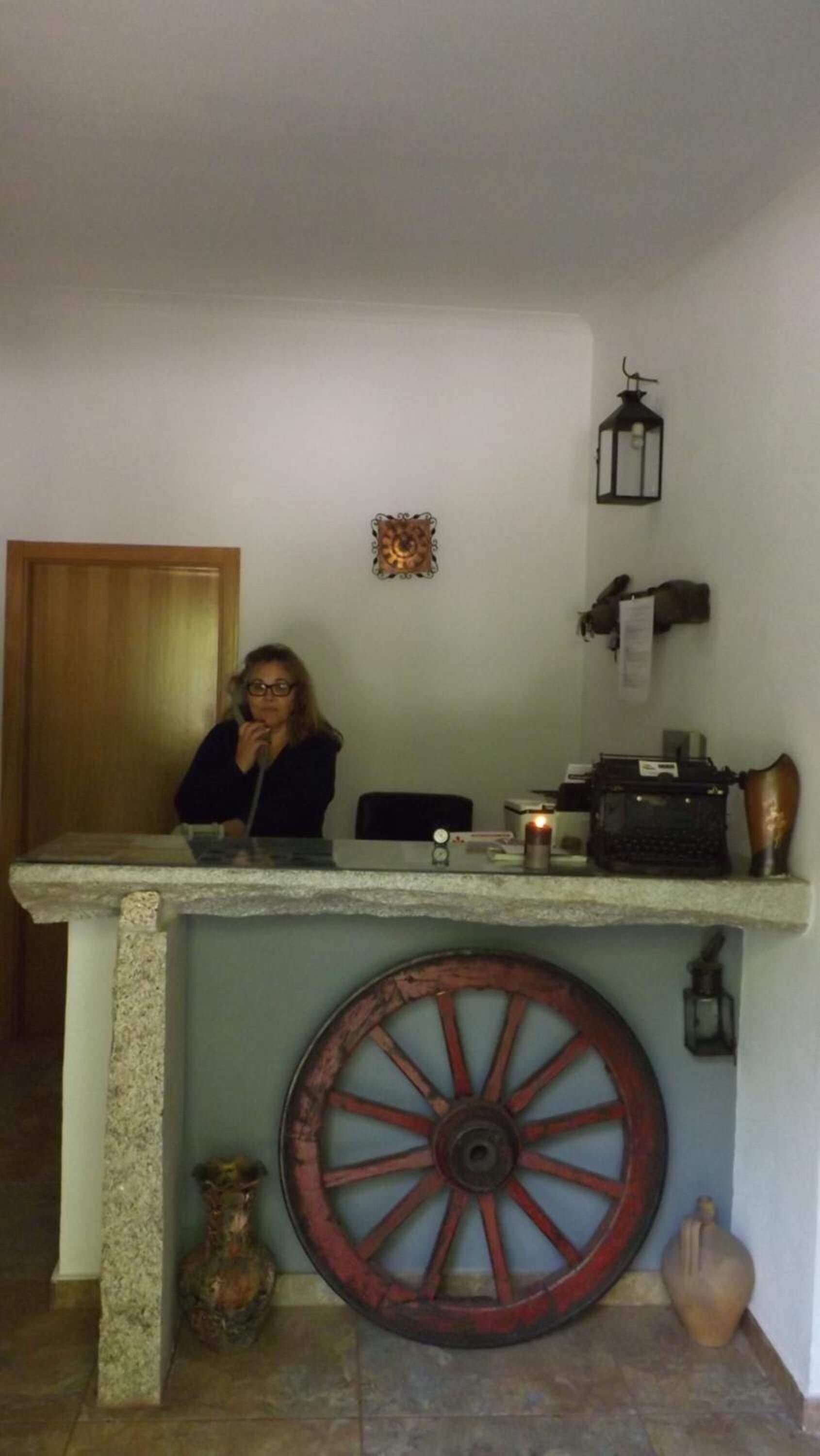 Um balcão de recepção com uma roda antiga, um relógio e um candeeiro na parede.