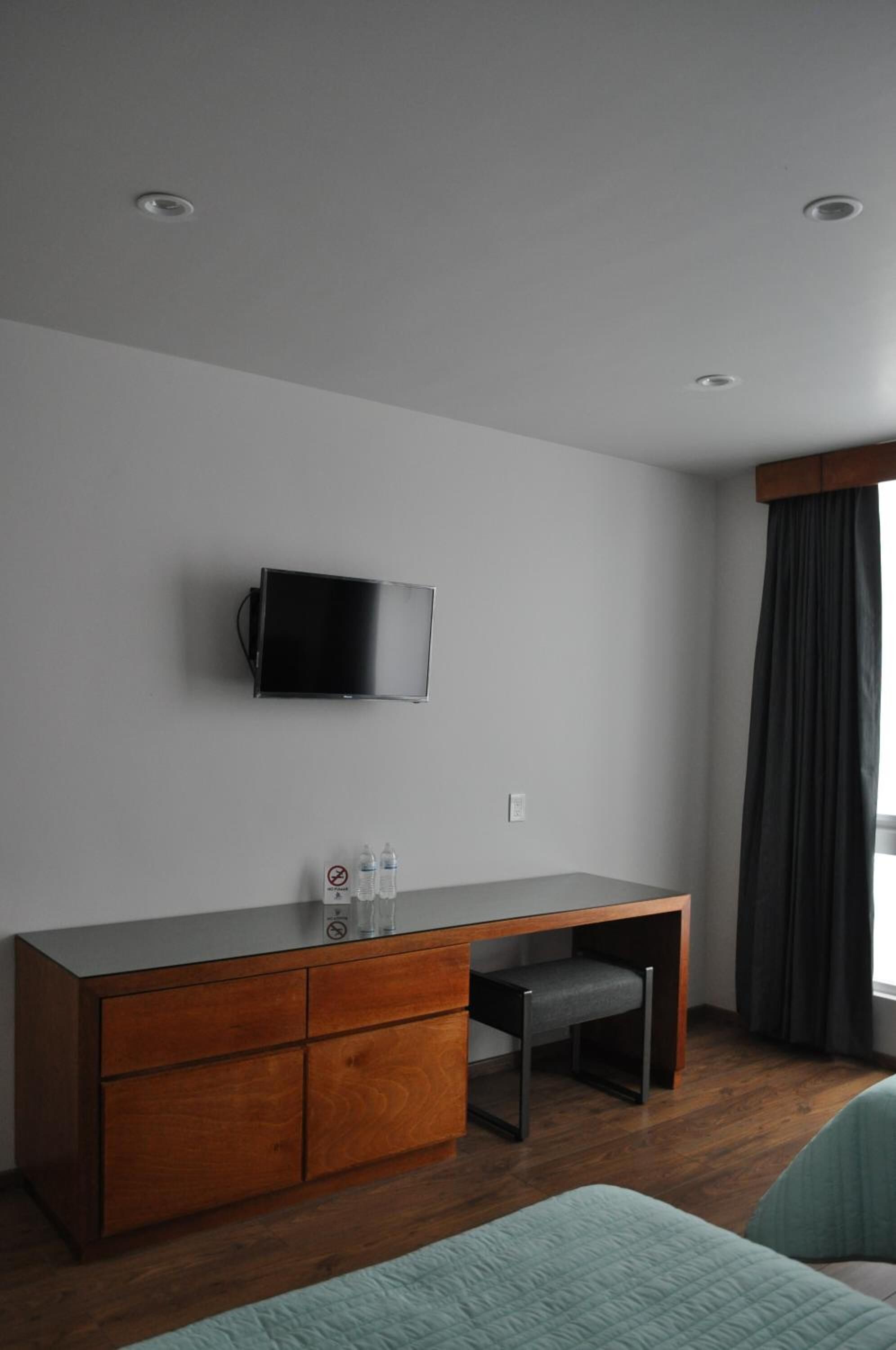 Quarto de hotel moderno com escrivaninha de madeira, televisão de tela plana, um banco e uma cama.