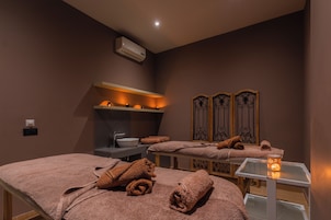 Sala de spa com duas mesas de massagem, uma pia e um espelho.