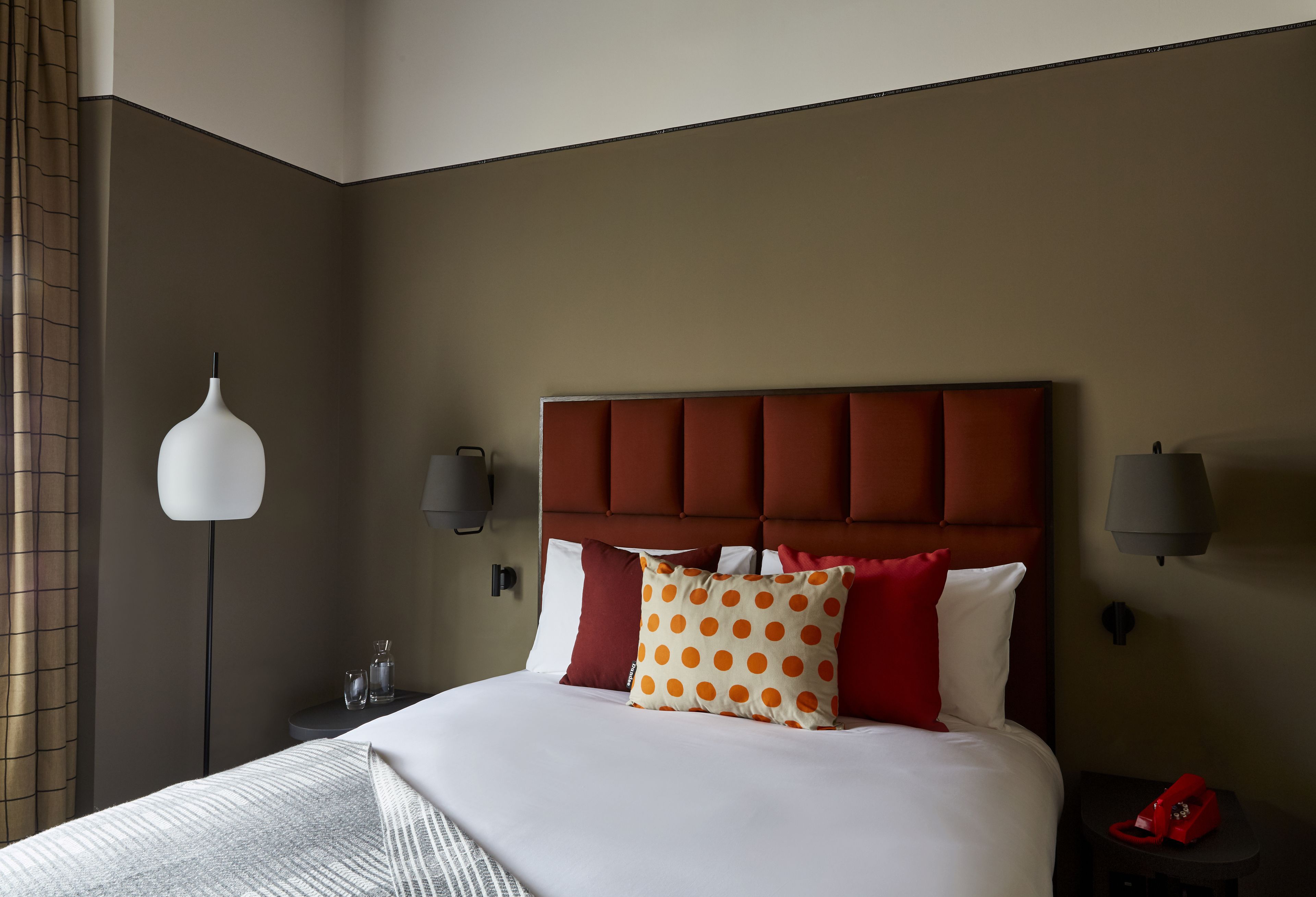 Quarto de hotel com uma cama grande, cabeceira, duas luminárias de apoio, mesa de cabeceira e telefone.