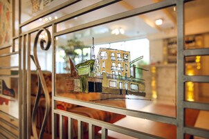 Uma maquete de um edifício com vários andares e varandas, vista através de uma janela com moldura de metal.