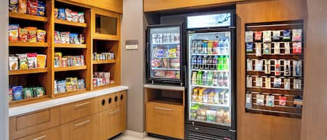 Uma área bem organizada para lanches e bebidas, com prateleiras repletas de petiscos e um refrigerador com bebidas.