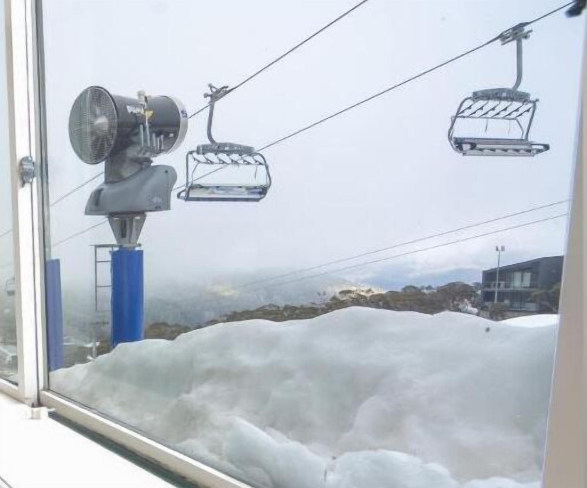 Vista pela janela de um teleférico com cadeira e paisagem coberta de neve.