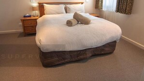 Quarto de hotel com cama grande, mesa de cabeceira, luminária, quadro na parede e janela com cortinas.