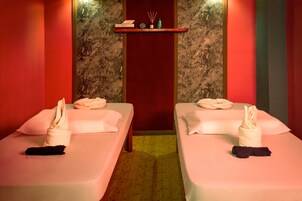 Duas camas de solteiro com toalhas e uma prateleira com relógio e velas em um quarto de spa.