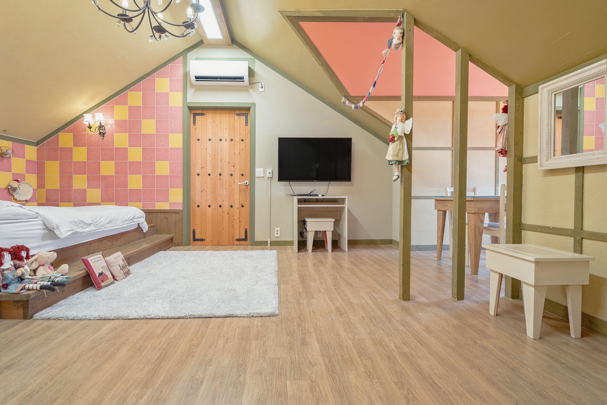 Quarto com teto inclinado, televisão, cama, escrivaninha e espelho.