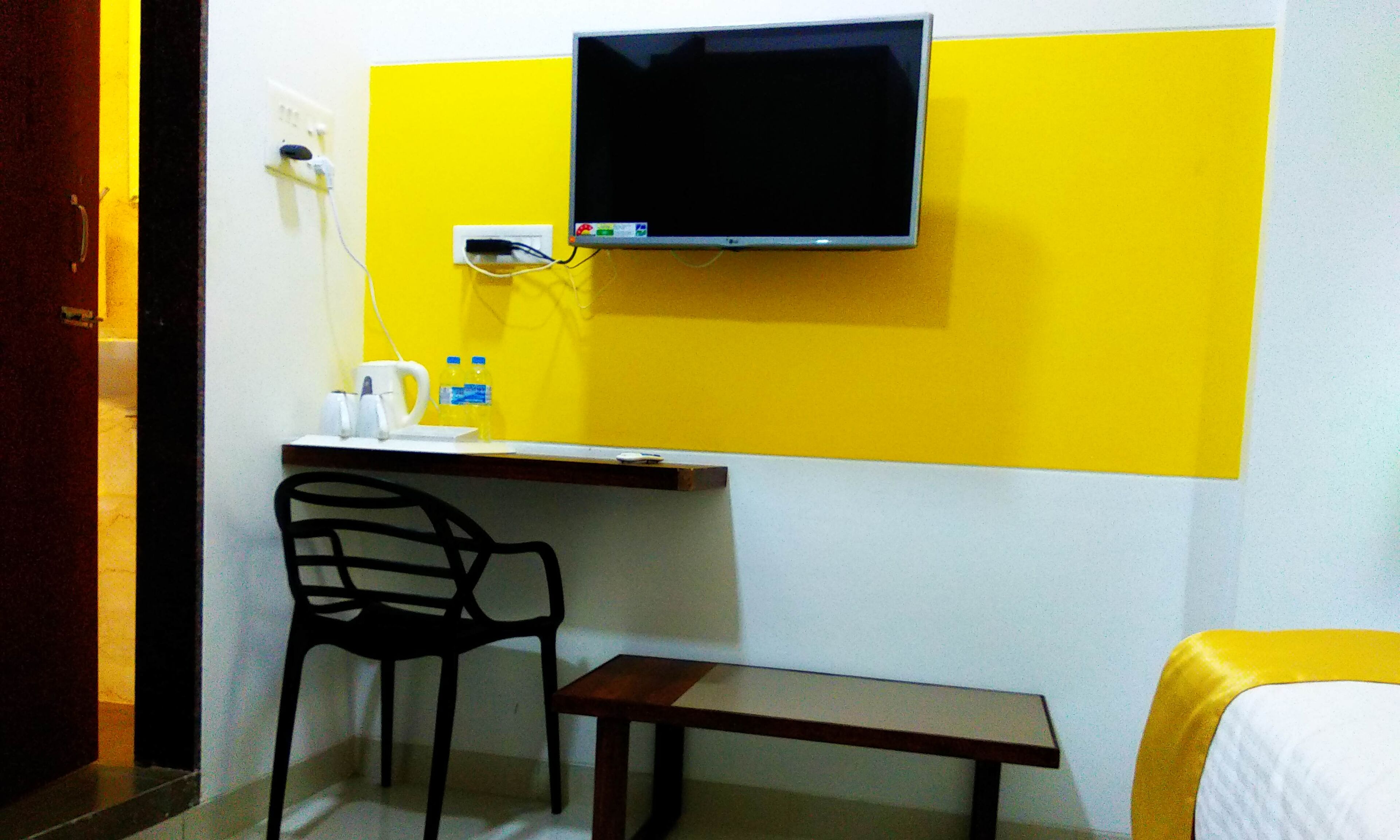 Quarto de hotel pequeno com escrivaninha, cadeira e televisão fixada na parede.
