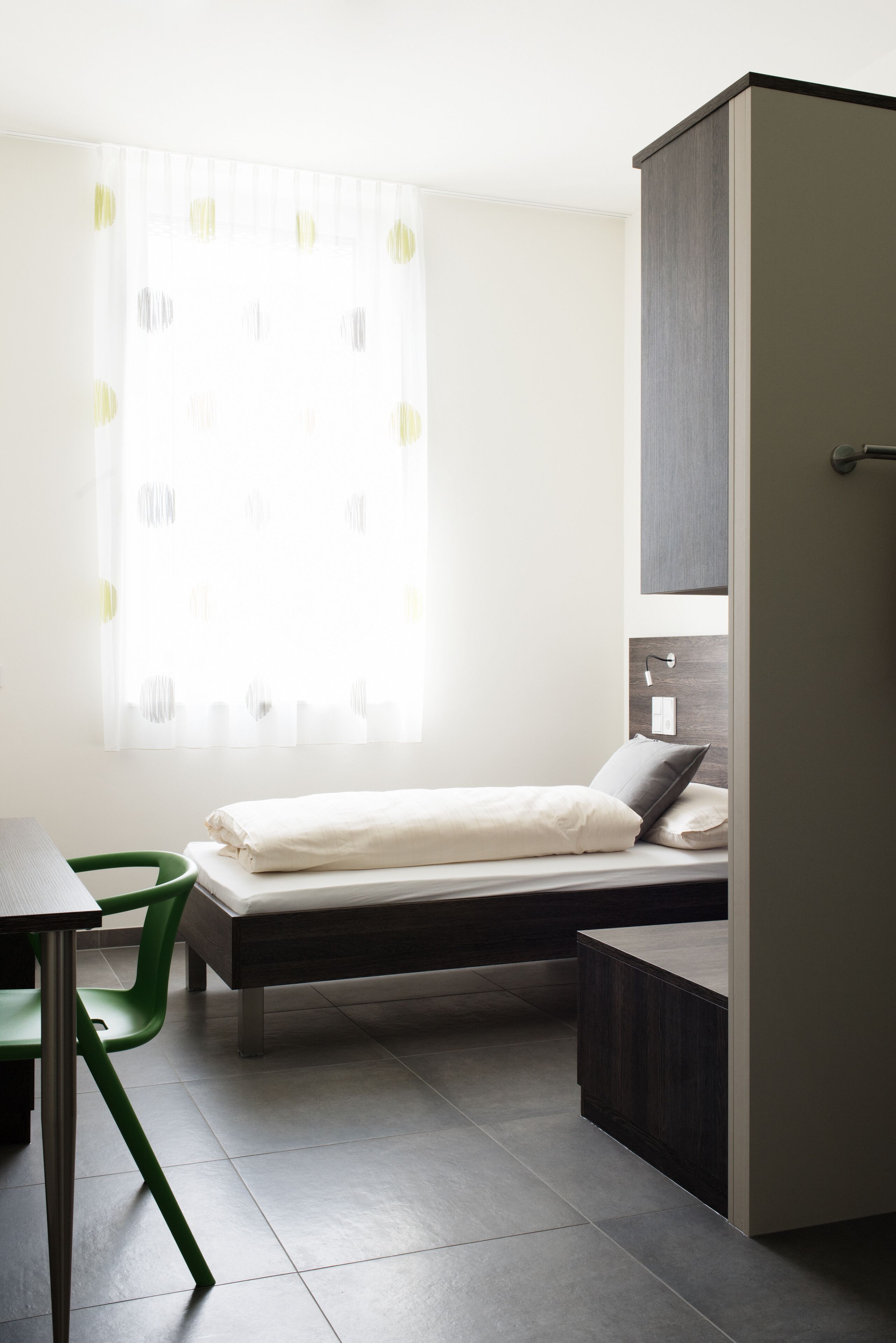 Quarto pequeno e moderno com uma cama, uma escrivaninha e uma cadeira.
