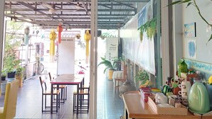 Uma área de refeições ao ar livre coberta, com mesa, cadeiras, plantas em vasos e lanternas penduradas.