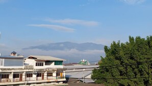 Um edifício com telhado plano e varanda, rodeado por vegetação.