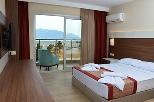 Quarto de hotel com cama, televisão, escrivaninha e vista para a praia e montanhas.