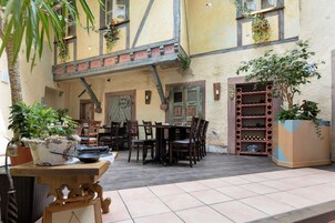 Uma área de refeições ao ar livre com mesas e cadeiras de madeira, um suporte para vinhos e plantas em vasos.