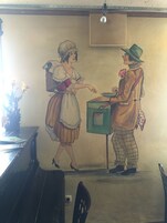 Um mural retrata um homem e uma mulher com roupas de época, uma mesa e uma cadeira.