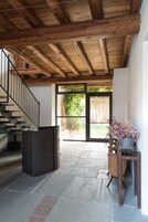 Um interior espaçoso com teto de madeira, uma escadaria e uma grande porta de vidro que dá para o exterior.