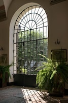 Quarto com uma grande janela arqueada, um lustre e plantas em vasos.