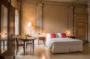 Quarto de hotel com uma cama grande, uma escrivaninha de madeira, um abajur e decorações elaboradas nas paredes.