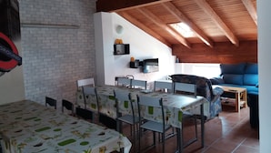 Uma área de refeições com parede de tijolos, vigas de madeira no teto e uma mesa com cadeiras.