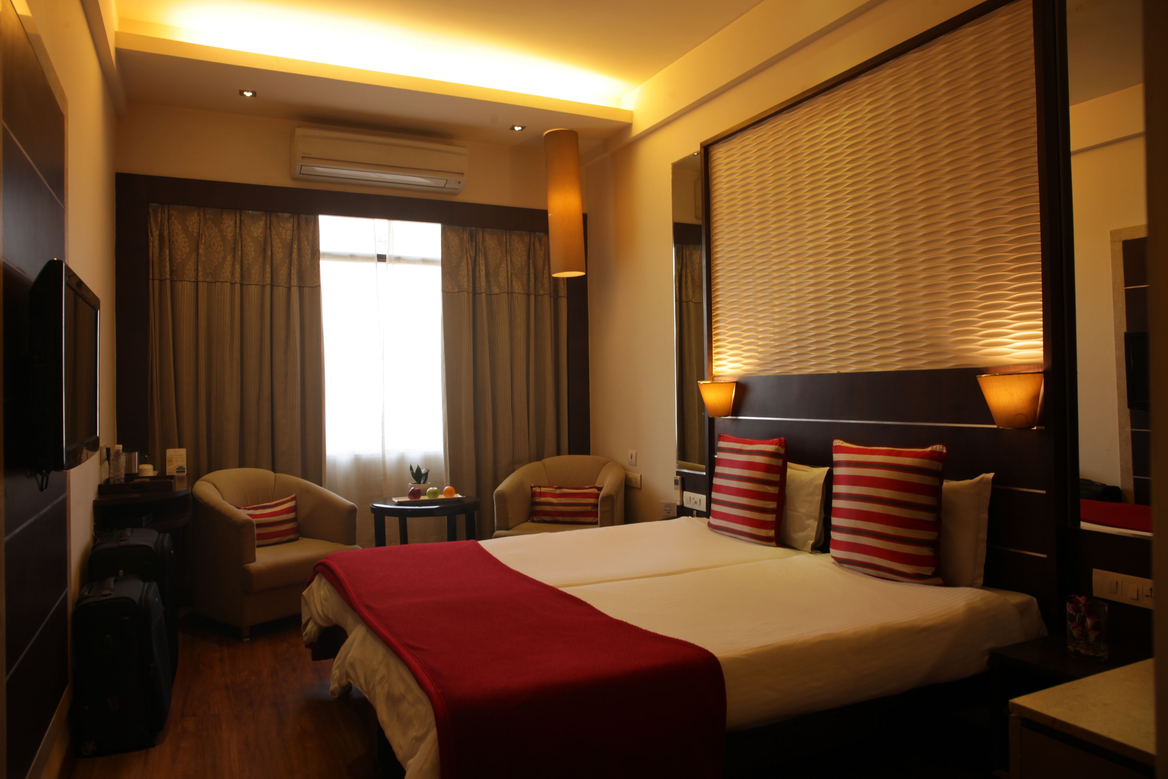 Quarto de hotel com uma cama grande, duas poltronas, uma mesinha e uma televisão.