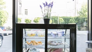 Vitrine refrigerada com diversos alimentos, uma planta em vaso e vista da rua.