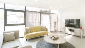 Uma sala de estar moderna com um sofá amarelo, um tapete cinza, uma TV de tela plana e um rack branco.