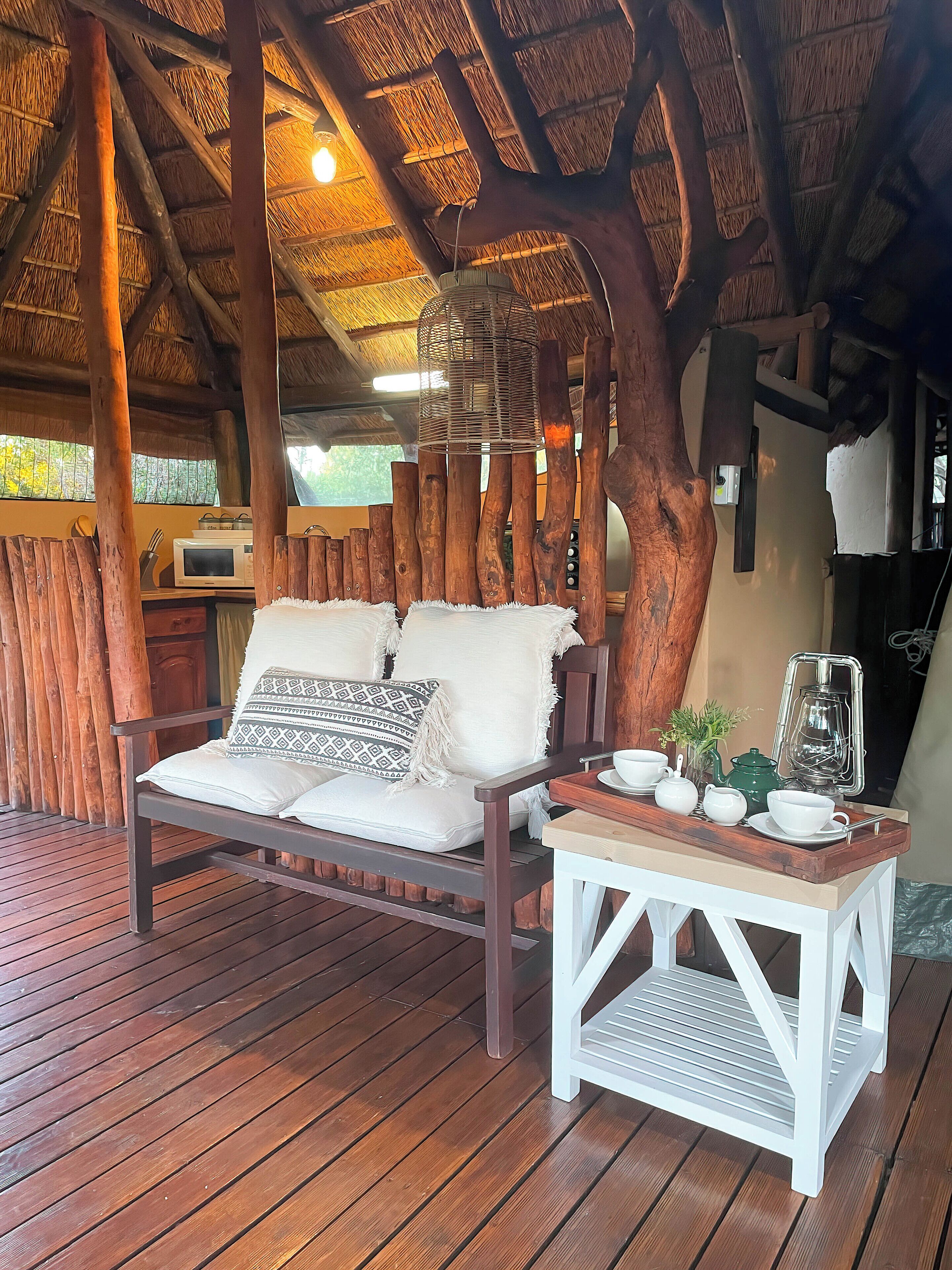Um deck de madeira com uma cama, uma mesa com conjunto de chá e uma estrutura de telhado de palha.