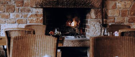 Lareira de tijolos com fogo aceso, cadeiras de vime e um menu em lousa.