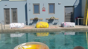 Uma área de piscina com dois sacos de feijão, um banco e uma parede com uma frase motivacional.