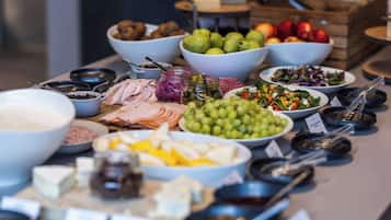 Uma mesa de buffet com diversos alimentos, incluindo carnes, queijos, frutas e saladas.