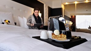 Quarto de hotel com uma cama, uma bandeja com uma fatia de torta, um copo de água e uma garrafa de água.