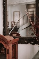 Uma escadaria com corrimão de madeira e vista para um quarto com porta e cadeira.