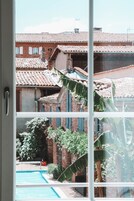 Visão pela janela de uma área residencial com piscina, edifícios de tijolo e uma bananeira.