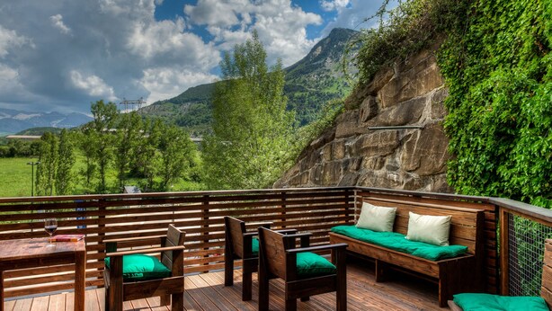 Um deck de madeira com assentos e uma mesa, com vista para uma paisagem montanhosa.