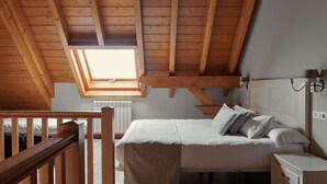 Quarto com teto de madeira, claraboia, cama com almofadas, mesa de cabeceira e criado-mudo.